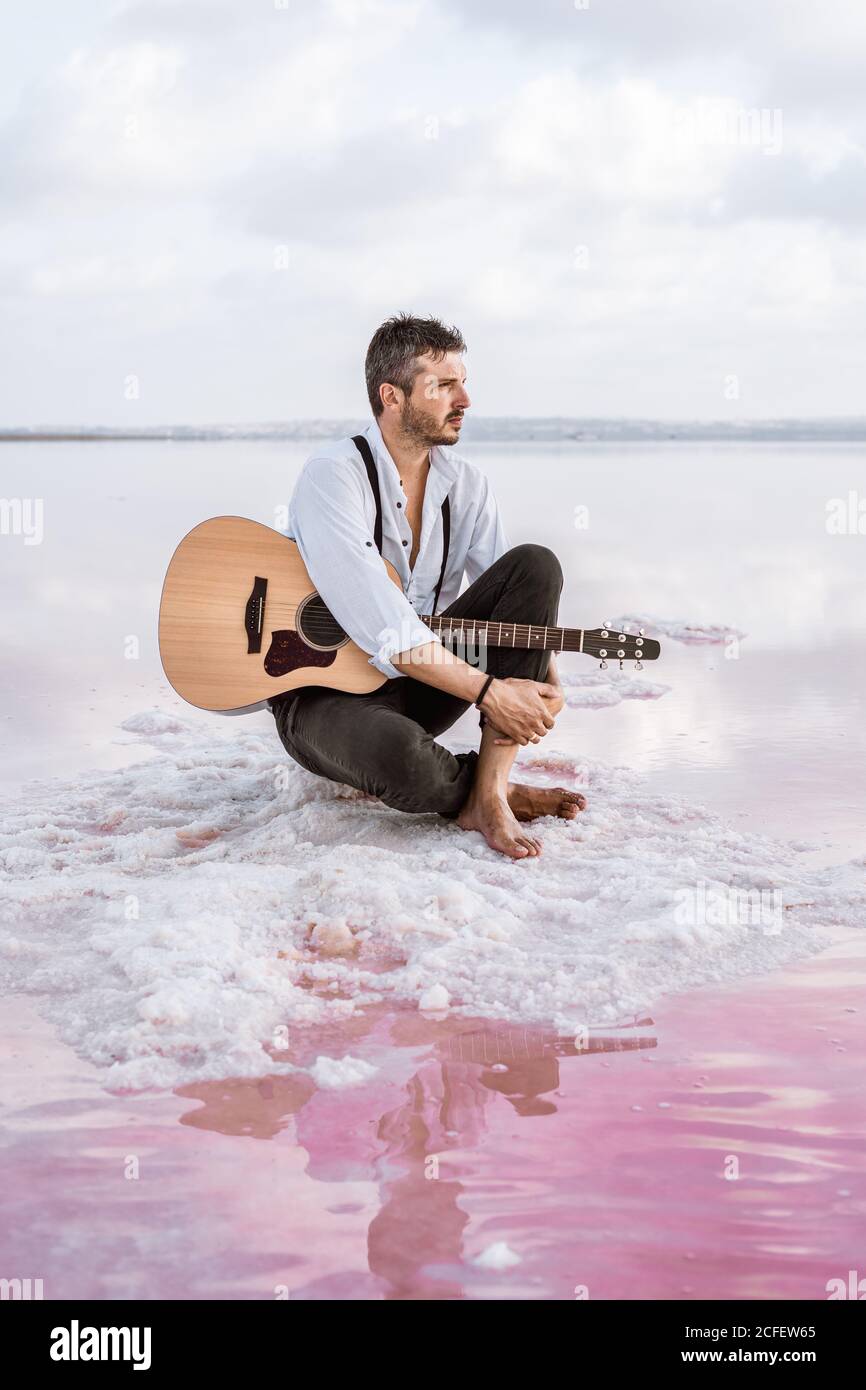 Wistful man in white shirt and suspenders carrying acoustic guitar and ...