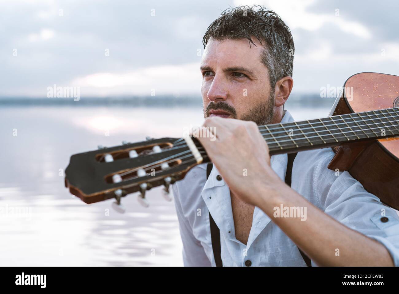 Wistful man in white shirt and suspenders carrying acoustic guitar and ...