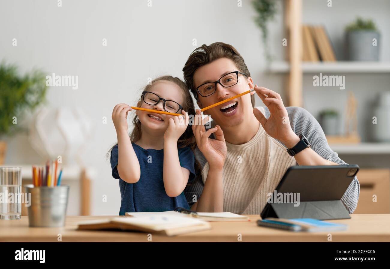 Back to school. Happy child and adult are sitting at desk. Girl doing ...