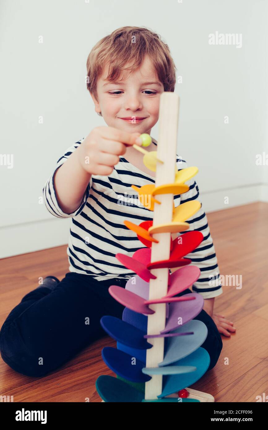 Funny smiling kid playing with toy tower and sitting on floor in room ...