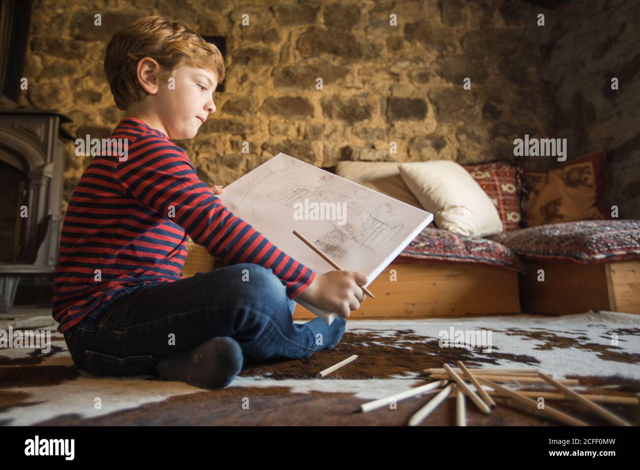 boy sitting on floor on cozy carpet and drawing with colored pencils in ...