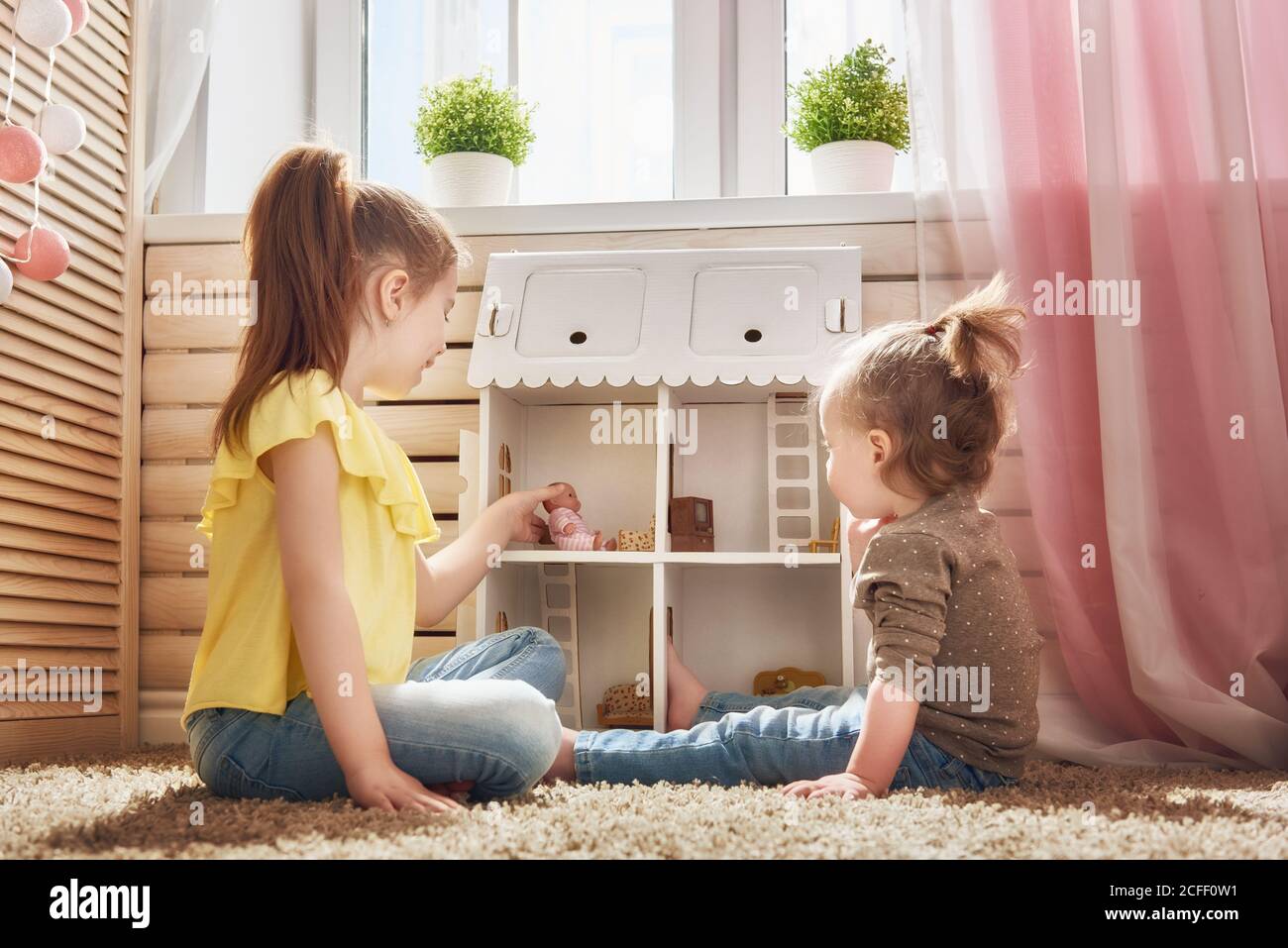 Happy sisters girls play with doll house at home. Funny lovely children ...
