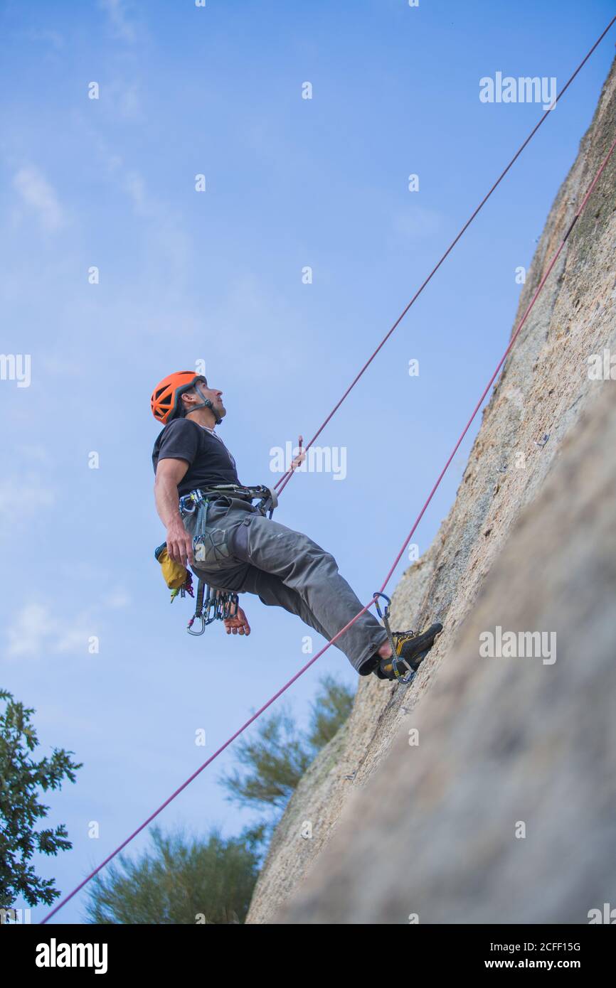 From below man climbing a rock in nature with climbing equipment Stock ...