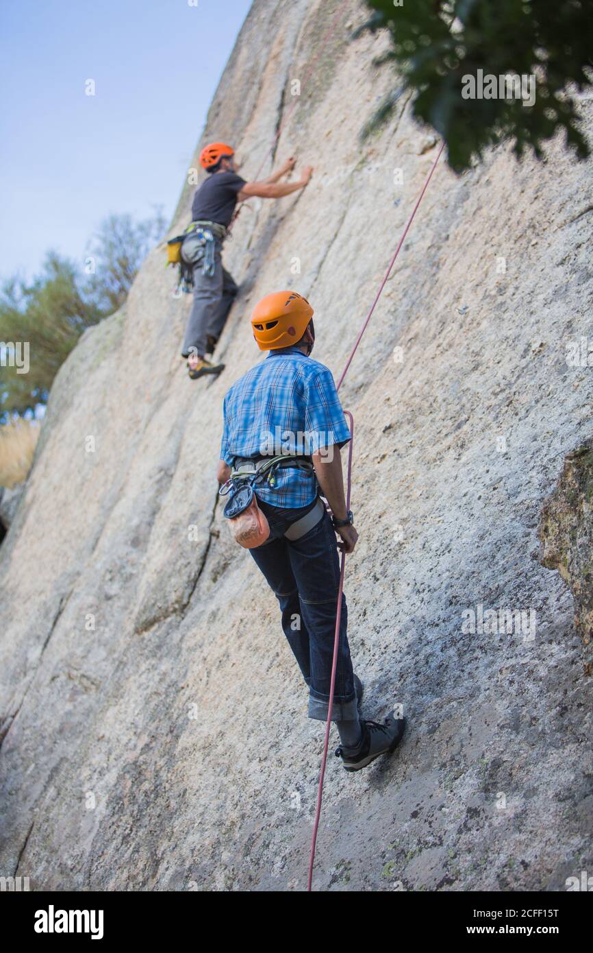 From below young adventurers climbing mountain wearing safety harness ...