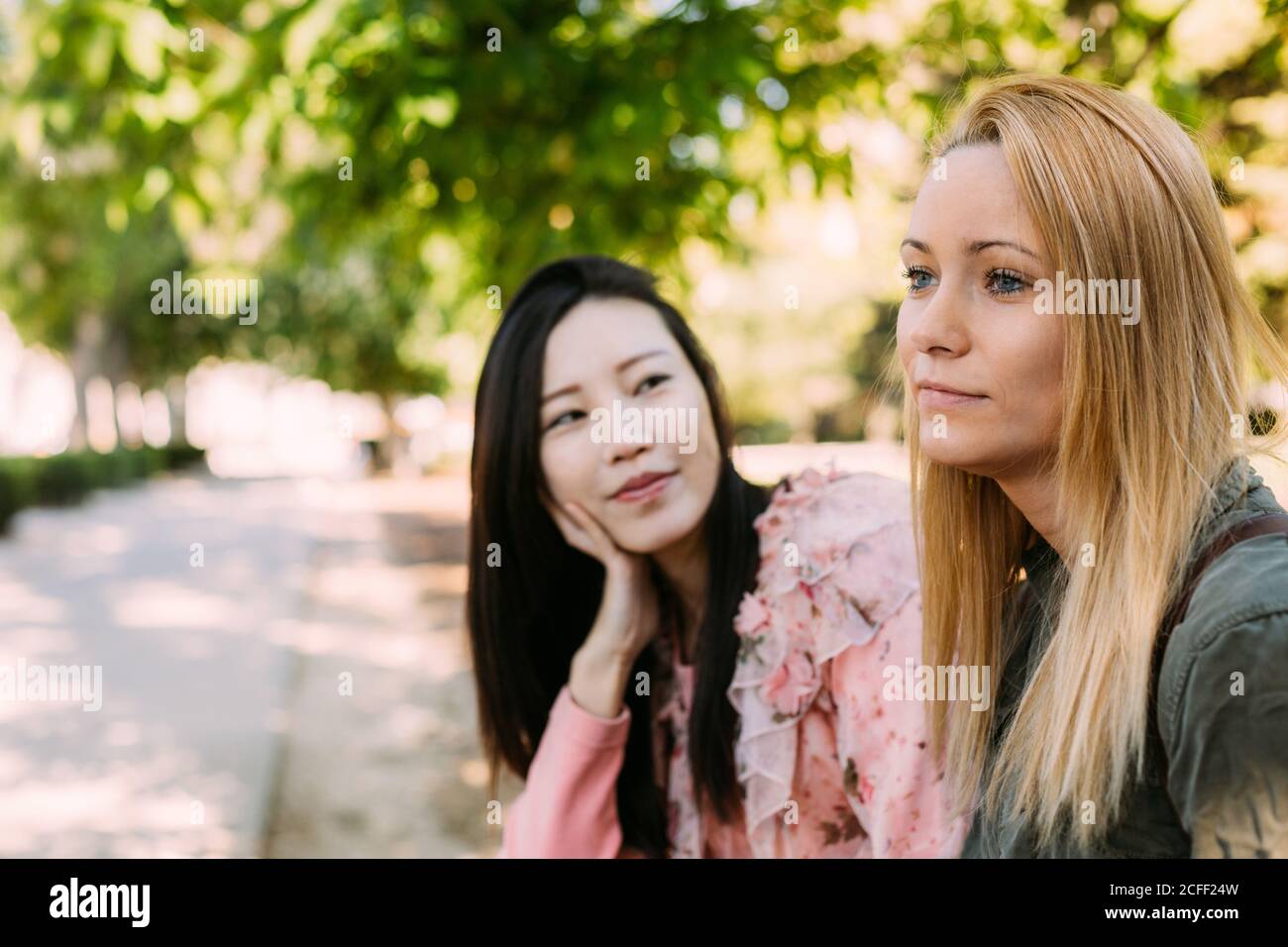 Two multiracial young women in casual outfits talking and looking at ...