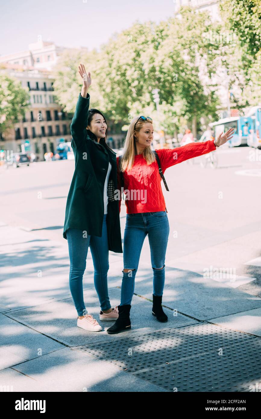 Happy multiracial ladies in stylish outfits smiling and waving hands ...