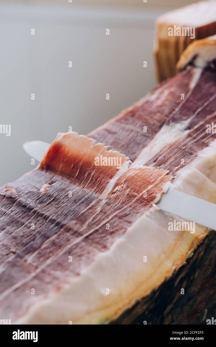 From above view of knife cutting thin slice of ham with tallow lines ...