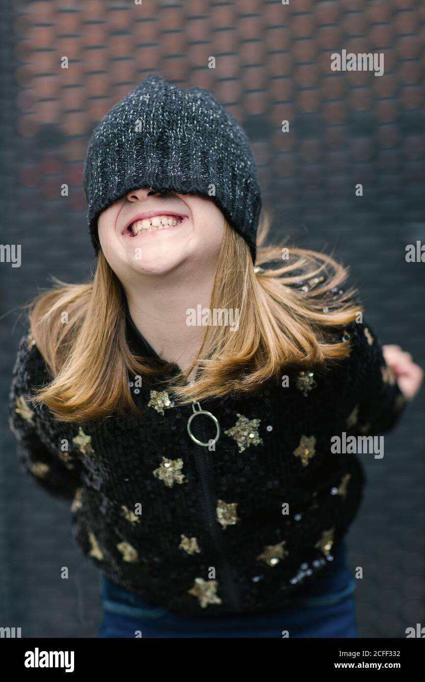 Funny anonymous kid in warm jacket and knitted cap covering half of ...