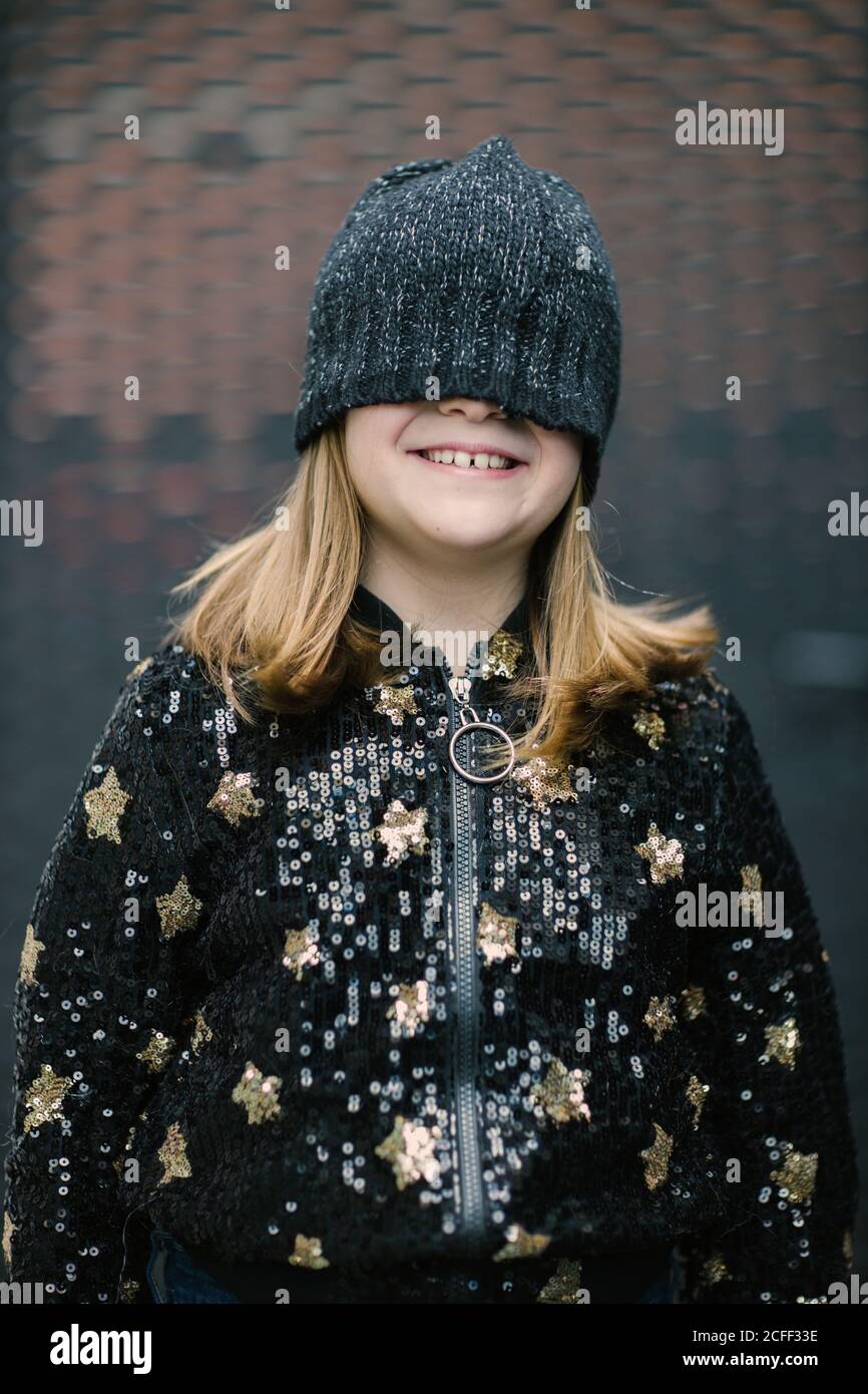 Funny anonymous kid in warm jacket and knitted cap covering half of ...