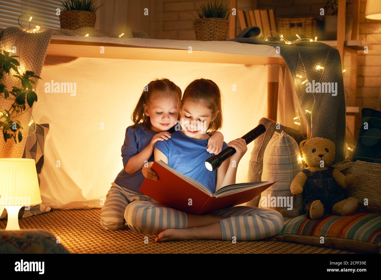Two cute little children are reading a book with flashlights in tent ...