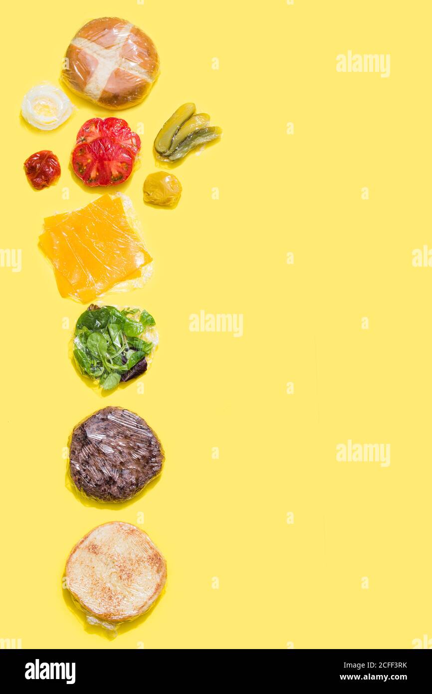Different ingredients of a cheese burger wrapped in plastic on yellow ...