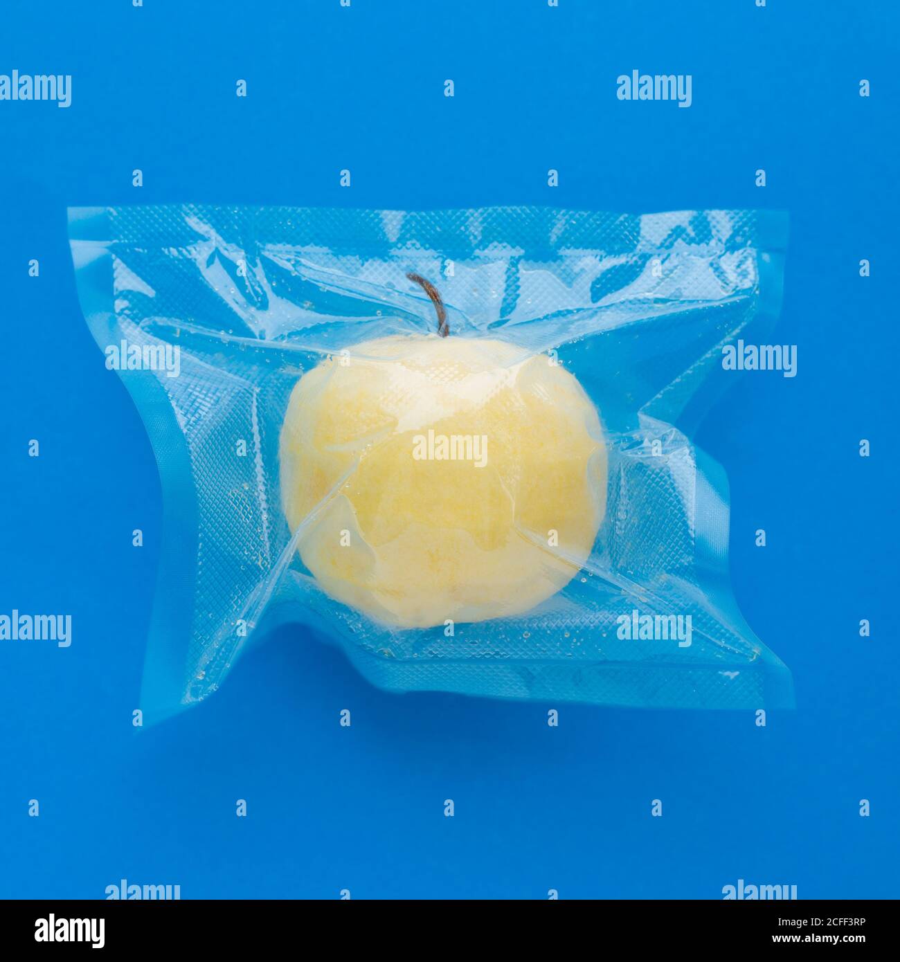 Top view of ripe yellow peeled apple in vacuum plastic bag on blue ...