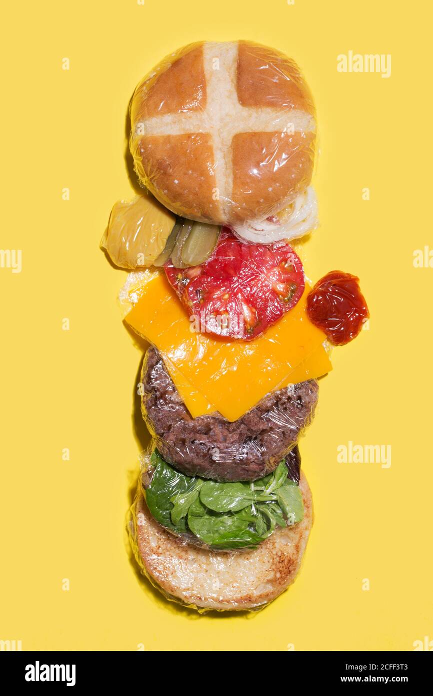Different ingredients of a cheese burger wrapped in plastic on yellow ...