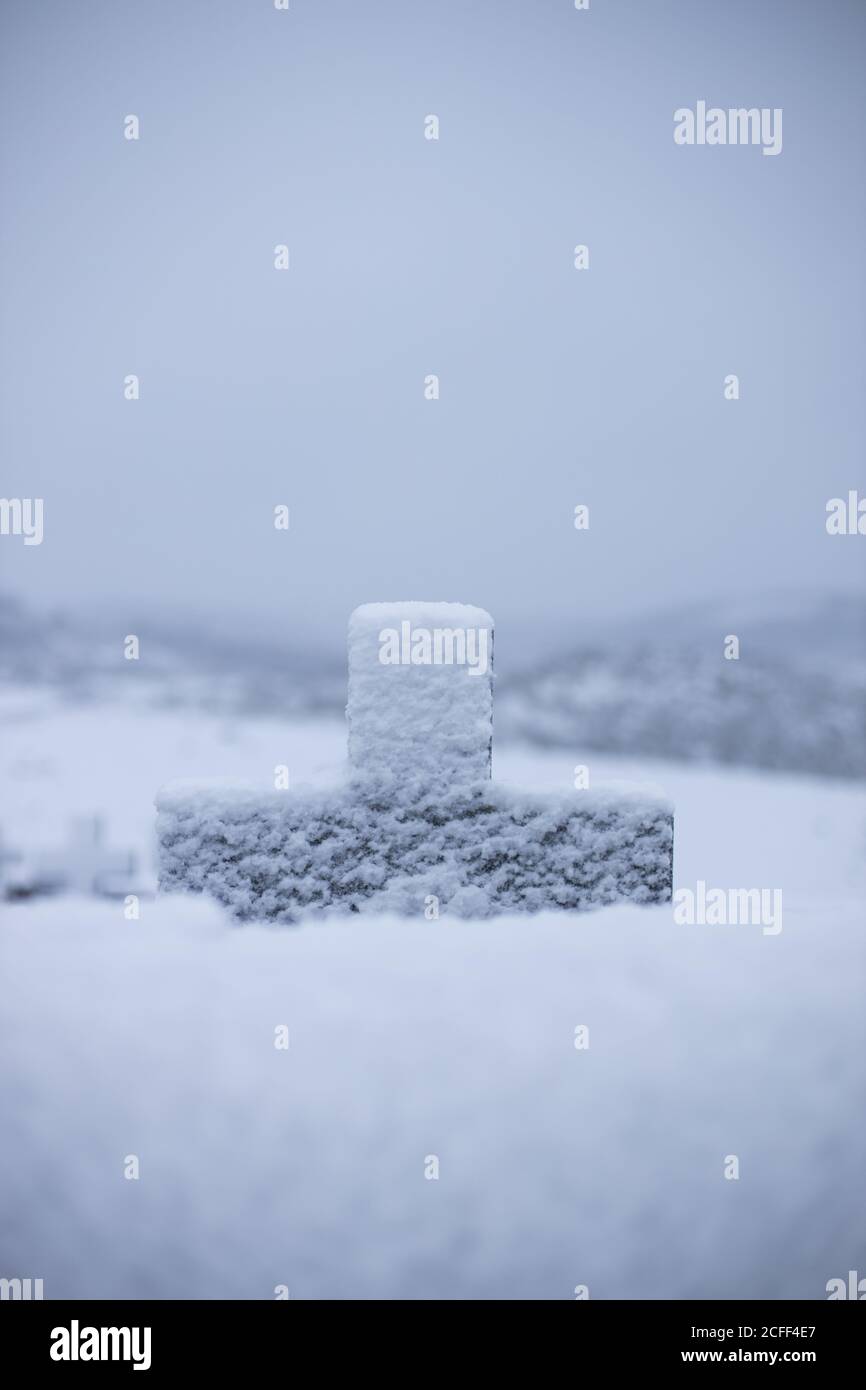 Wooden snowbound cross near rocks with snowy empty field and grey ...