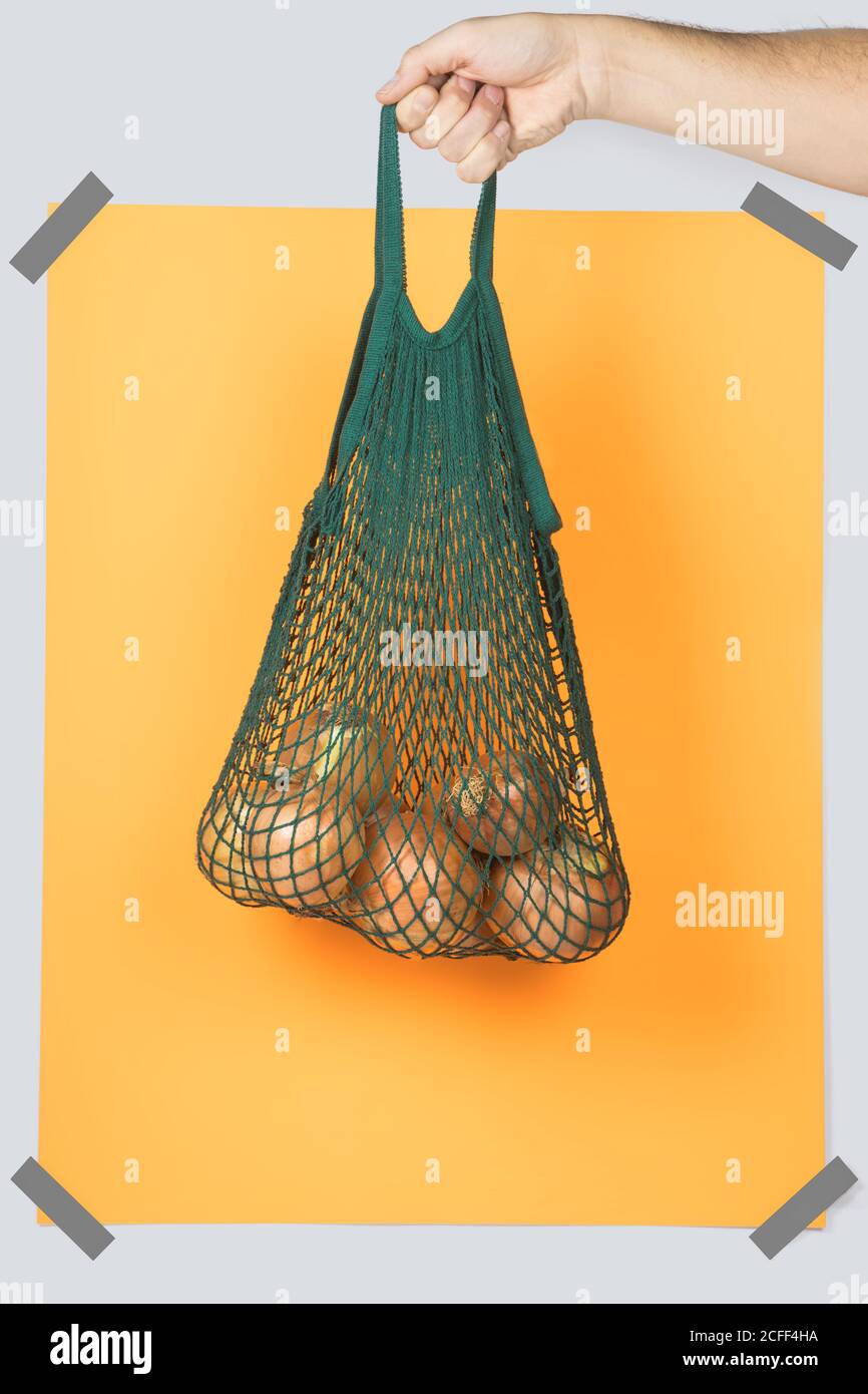 anonymous person carrying green string bag with ripe onions against ...