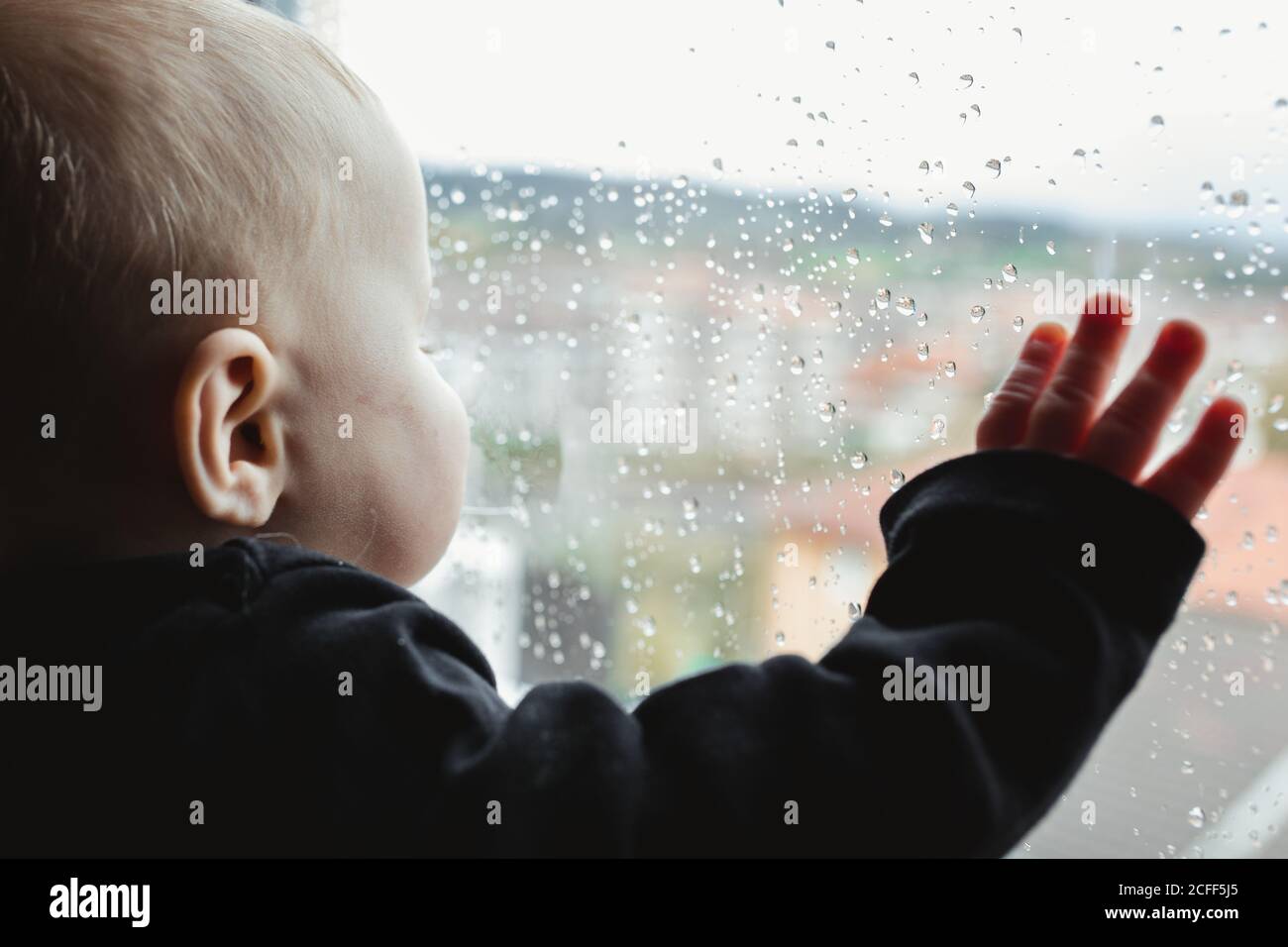 anonymous baby looking out wet window Stock Photo - Alamy