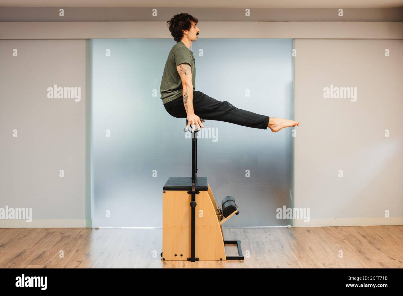 Side view of strong sportsman balancing on hands on pilates chair ...
