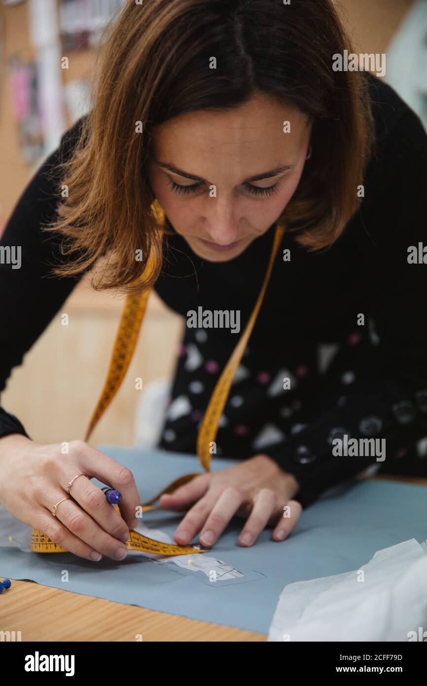 Adult lady using tape to measure garment part on table during work in ...