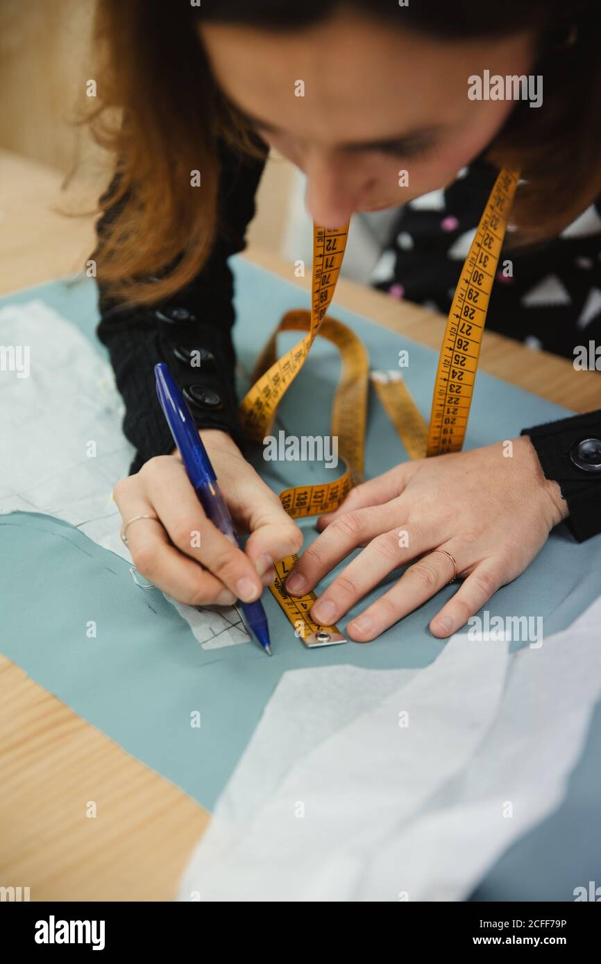 Adult lady using tape to measure garment part on table during work in ...