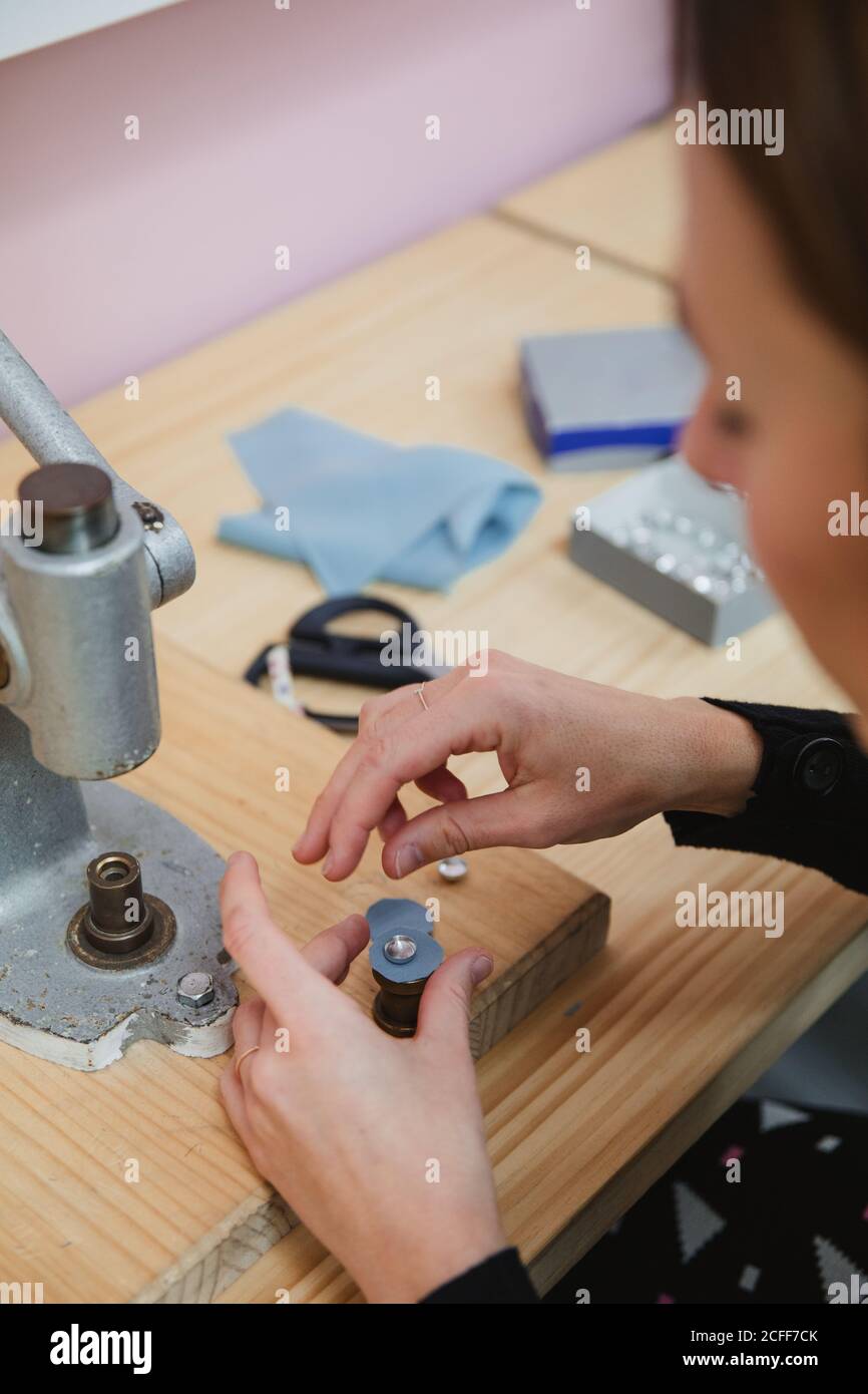 Crop anonymous person hands pulling lever of button maker on table in ...