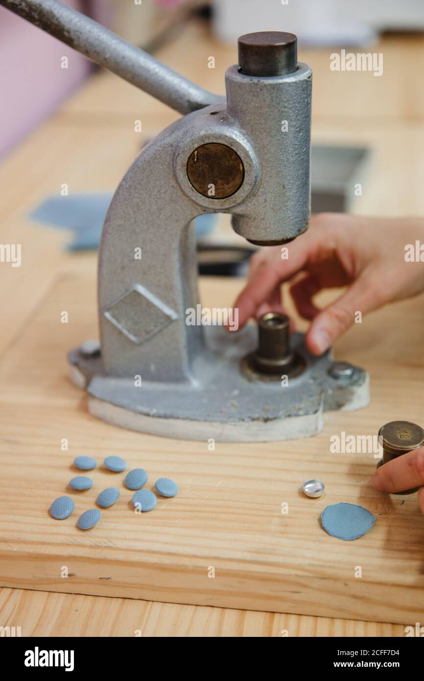 Crop anonymous person hands pulling lever of button maker on table in ...