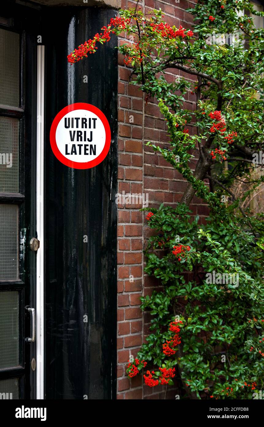 Black door frame with a "Keep exit clear" sign in Dutch and a bush with ...
