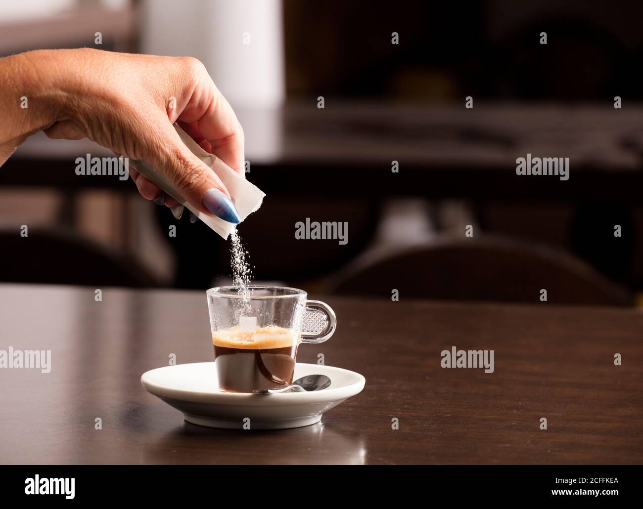 female hand with sugar envelope dumped into coffee cup, on top of ...
