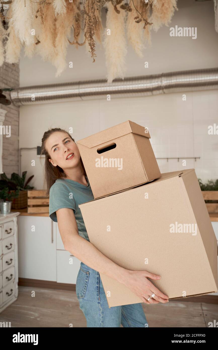Side view of young Woman making effort and carrying cardboard boxes ...