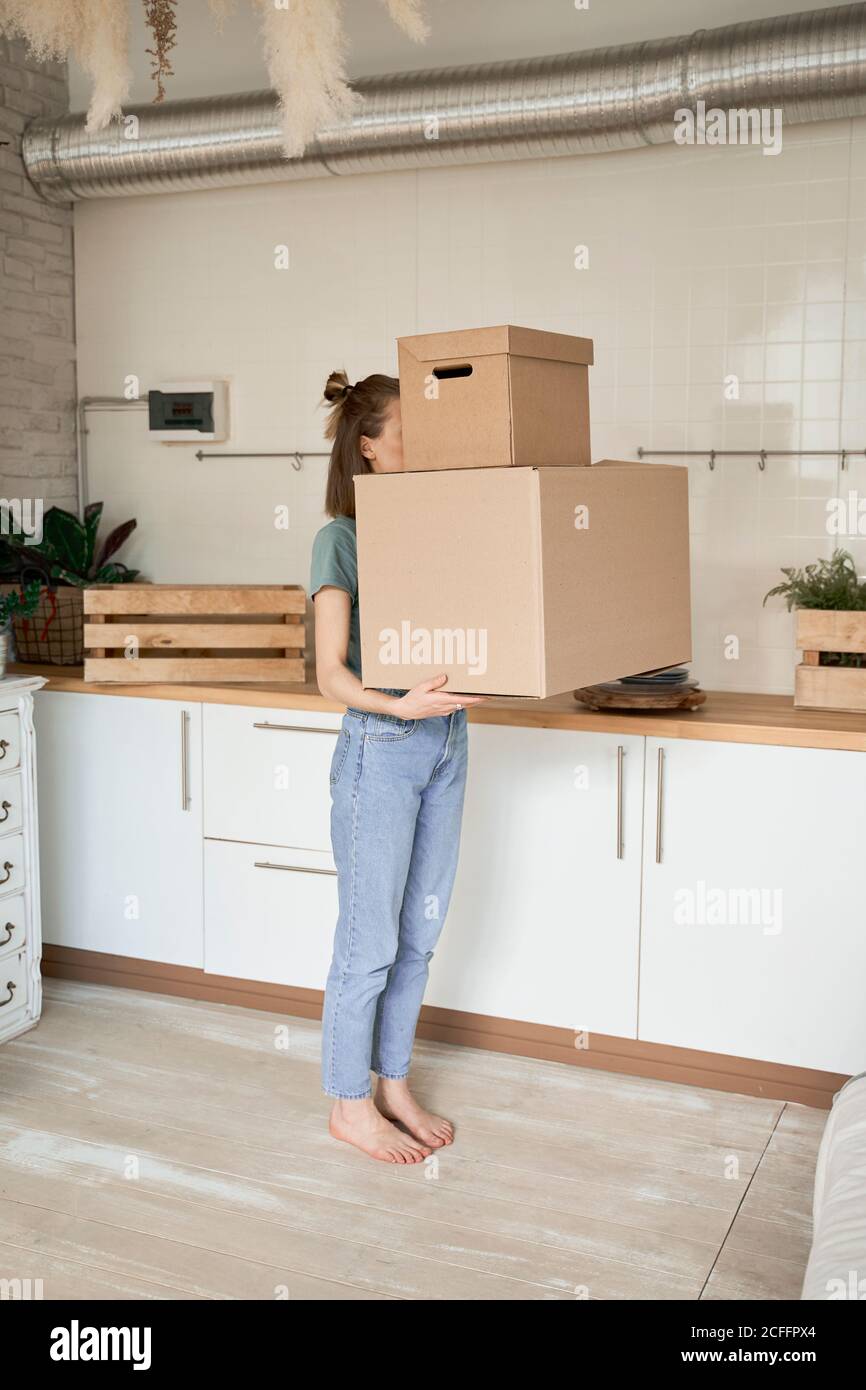 Side view of anonymous young Woman making effort and carrying cardboard ...