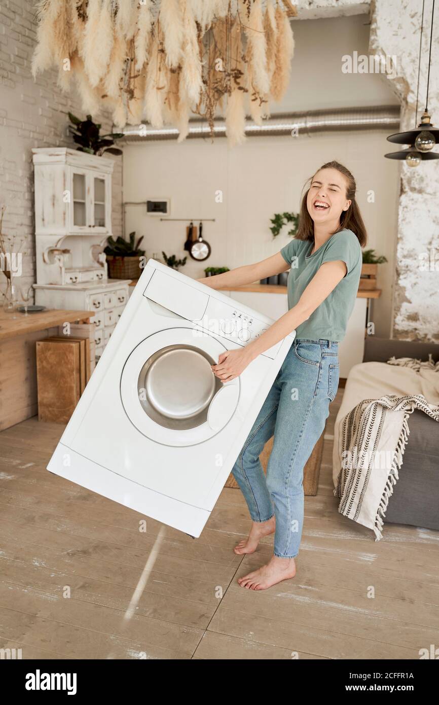 Powerful cheerful young Woman trying to carry white washing machine ...