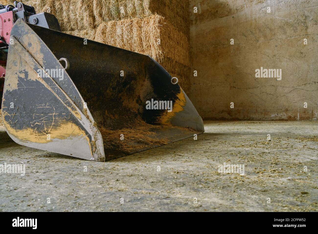 Side view of big heavy bucket of tractor placed on dirty floor near hay ...