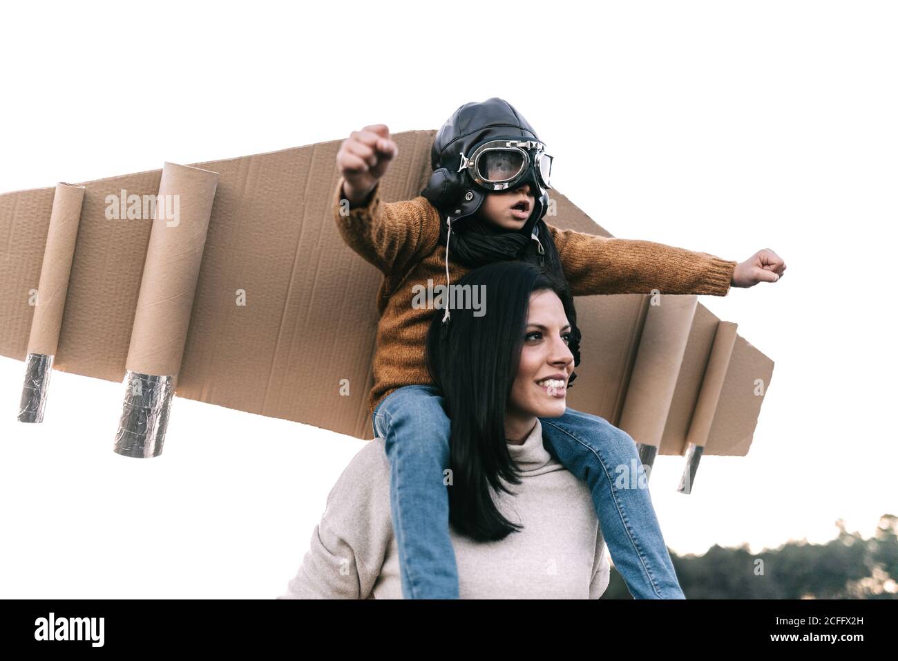 Happy cute boy wearing goggles and cardboard wings while sitting on ...