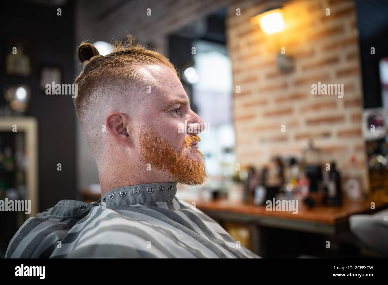 side view of redhead man sitting in modern barbershop waiting for ...