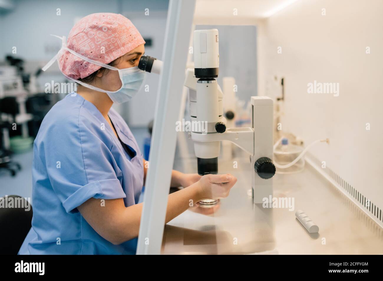 From above doctor in medical mask and uniform injecting ovum on Petri ...