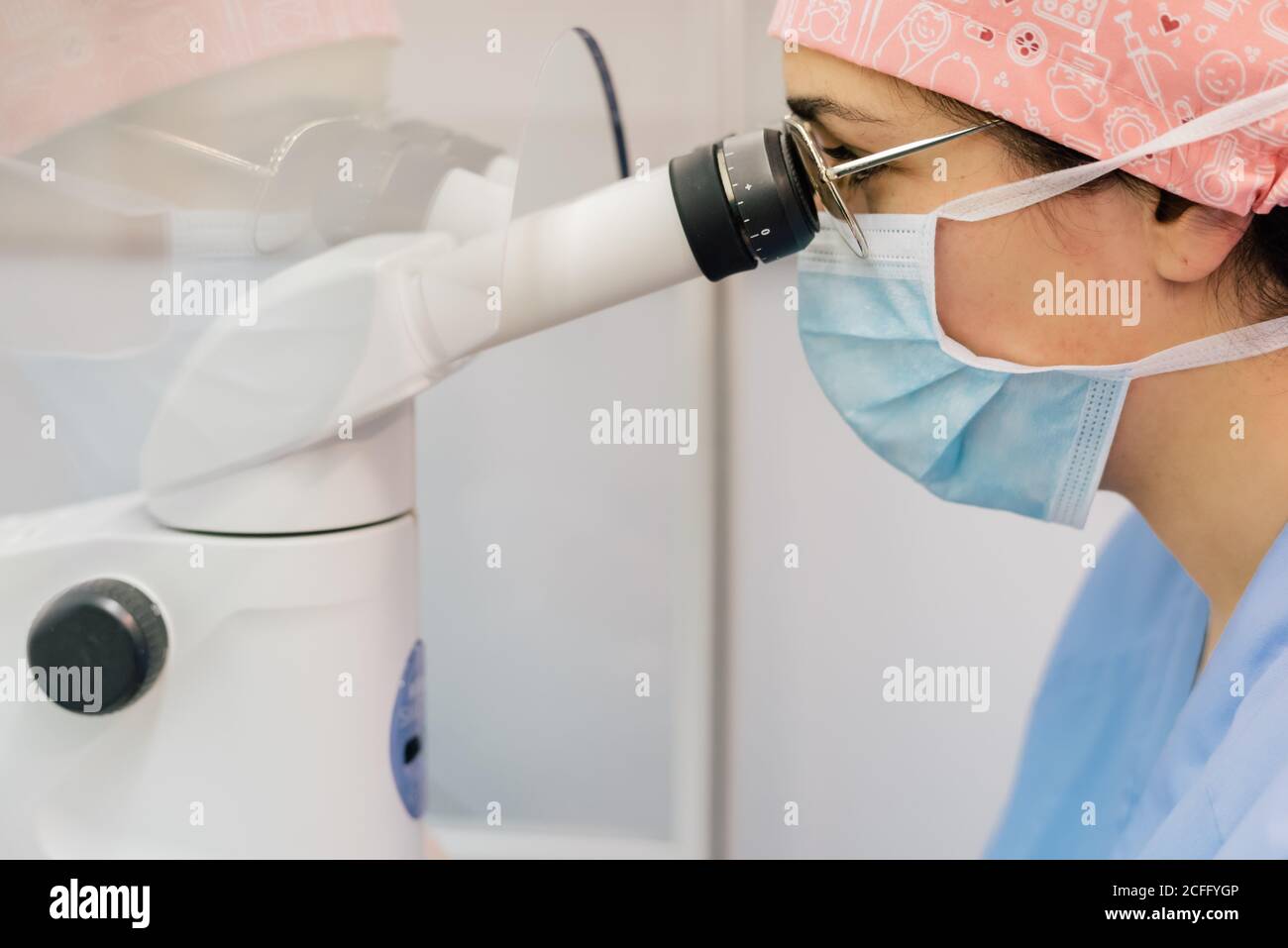 Side view of Woman in medical uniform and mask using modern microscope ...