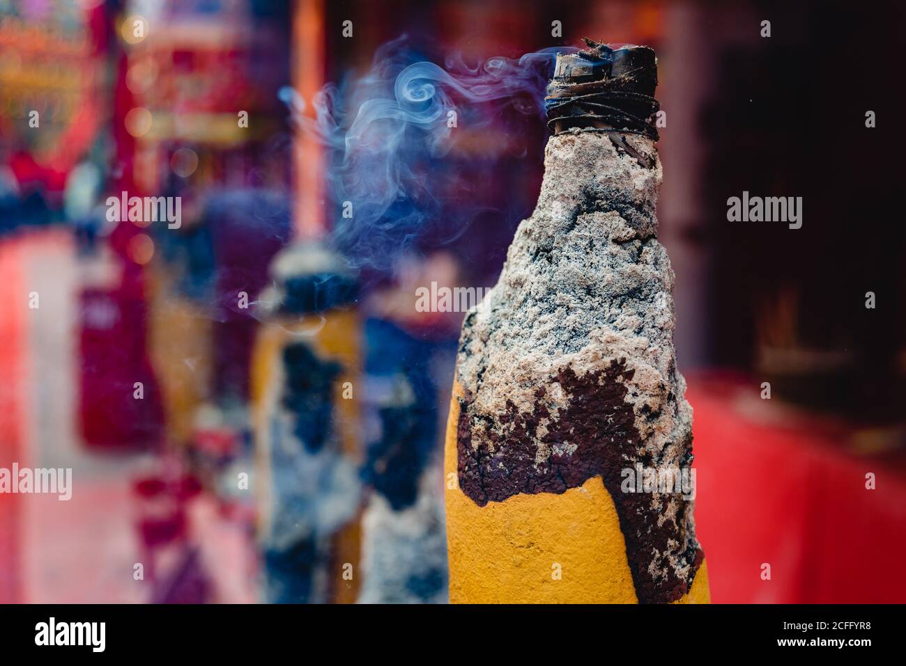 Yellow colored big incense stick smoking slightly outside of temple in ...