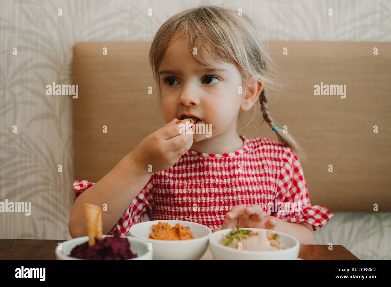Cute little girl eating assorted tasting appetizing snack at table ...
