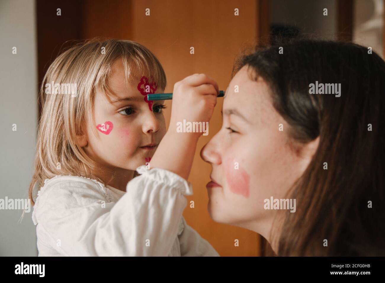 Side view of little girl painting face of teen sister while having fun ...