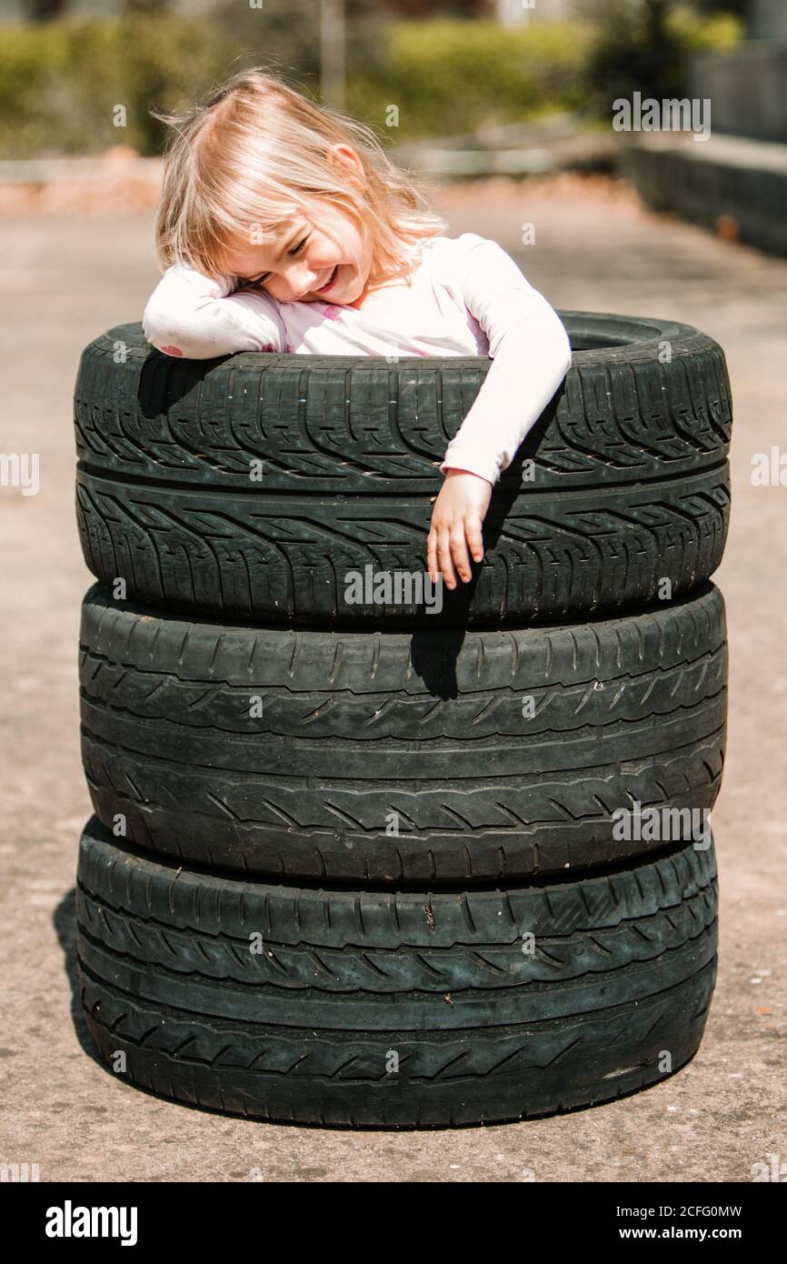 Happy adorable little girl resting in stack of car tires while having ...