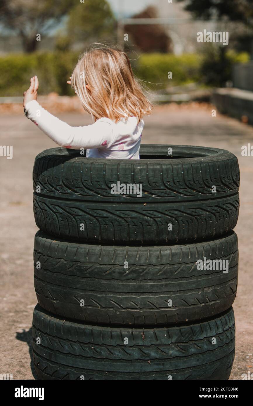 From Behind anonymous of little girl standing in stack of car tires ...