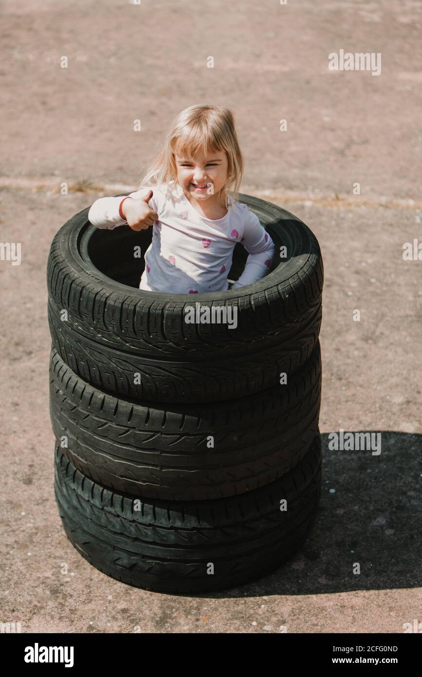 From above of happy adorable little girl standing in stack of car tires ...