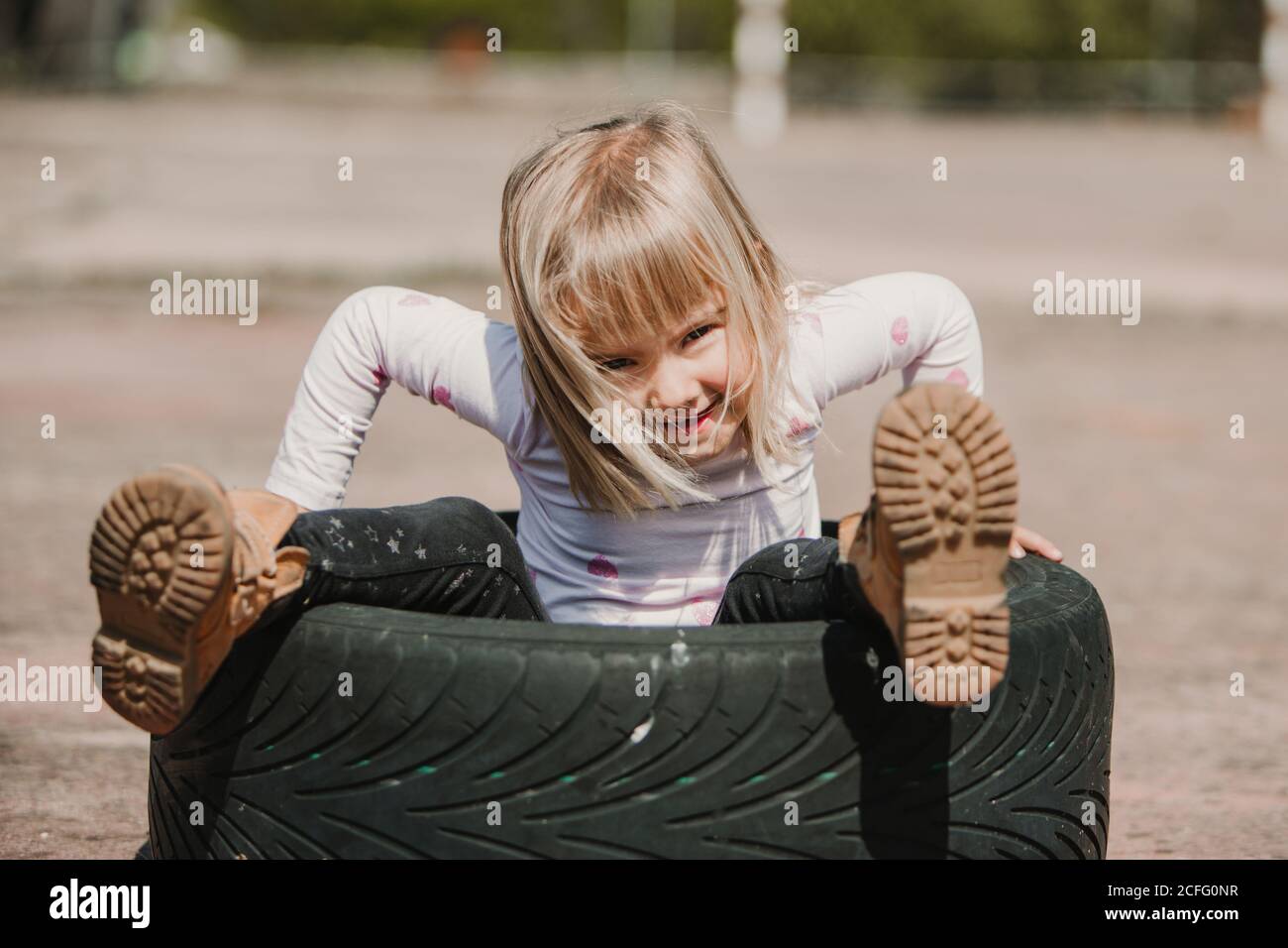 From above of happy adorable little girl sitting inside car tire while ...