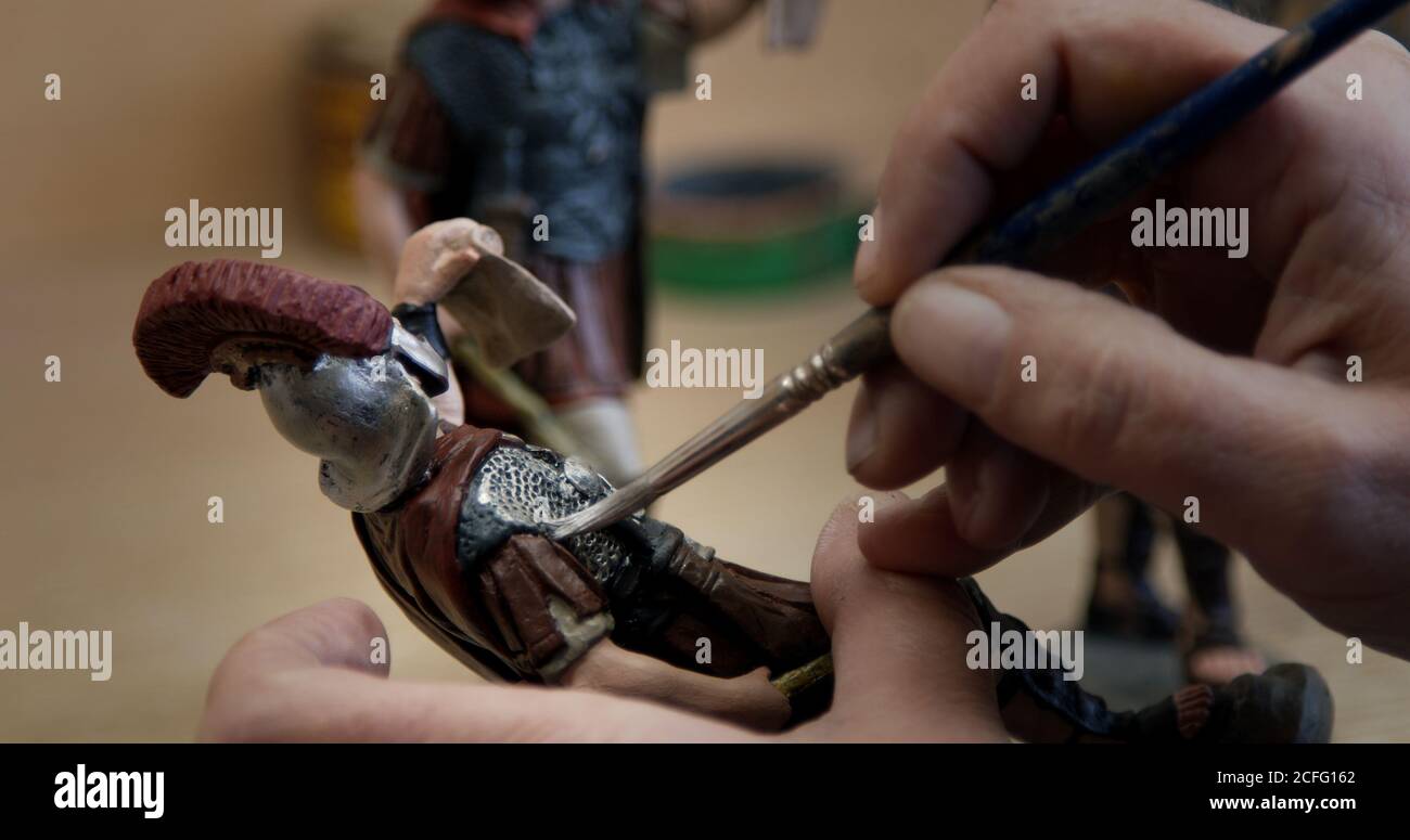 Side view of crop person painting clay figurines of soldiers with brush ...