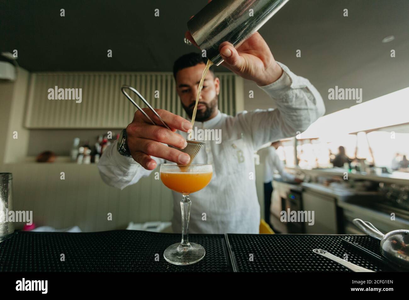 Cheerful man pouring cocktail and alcoholic drinks from shaker in a bar ...