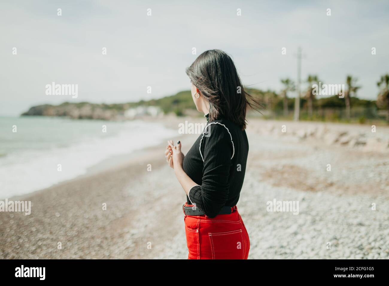 Side view of stylish Woman admiring view of calm sea while standing on ...