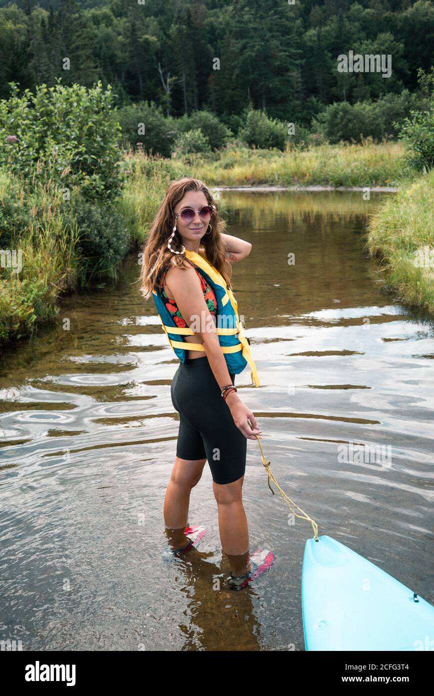 Female traveler with kayak standing in clean water of river and ...