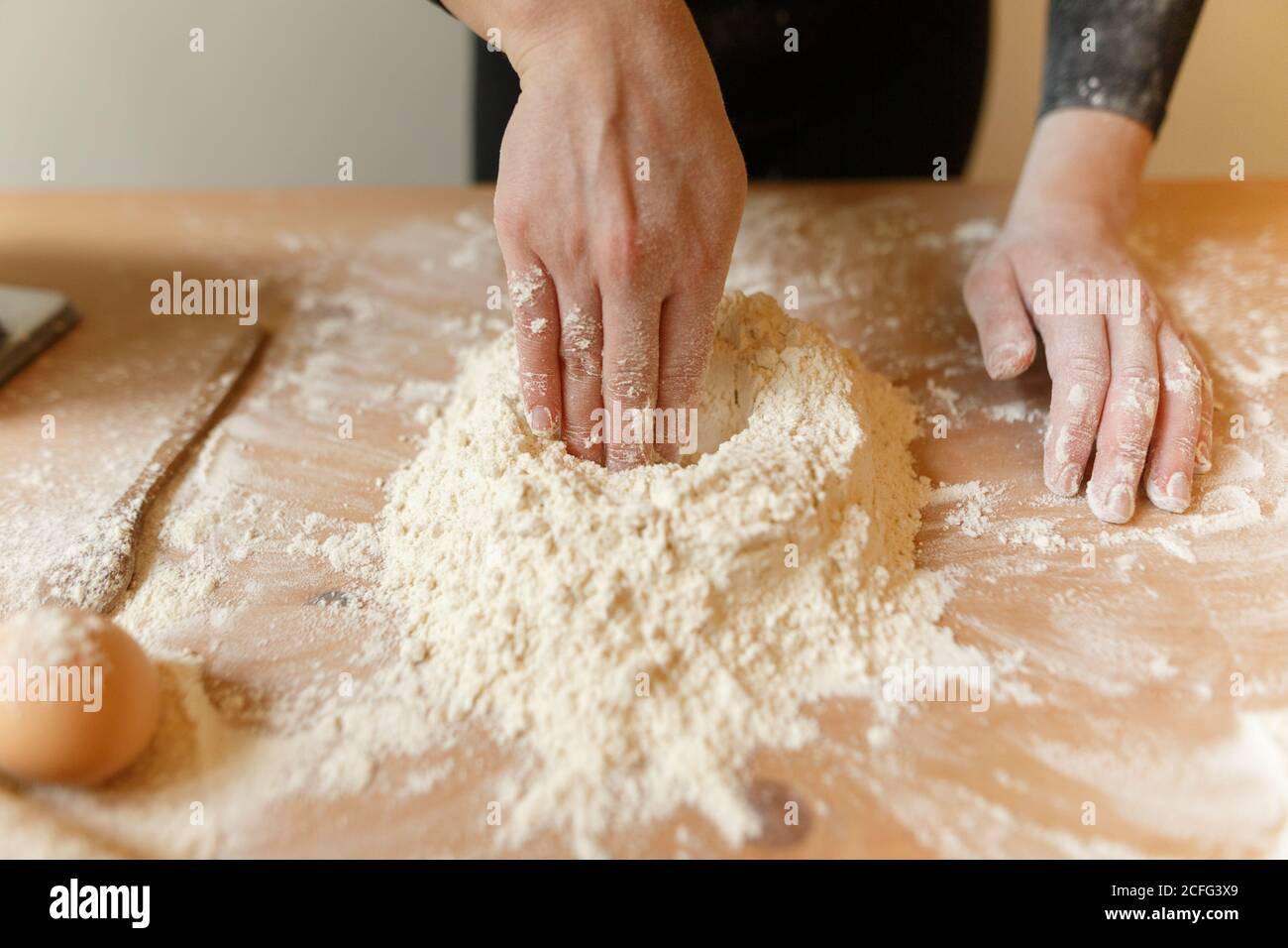 anonymous person in black clothes making recess in flour mass with hand ...