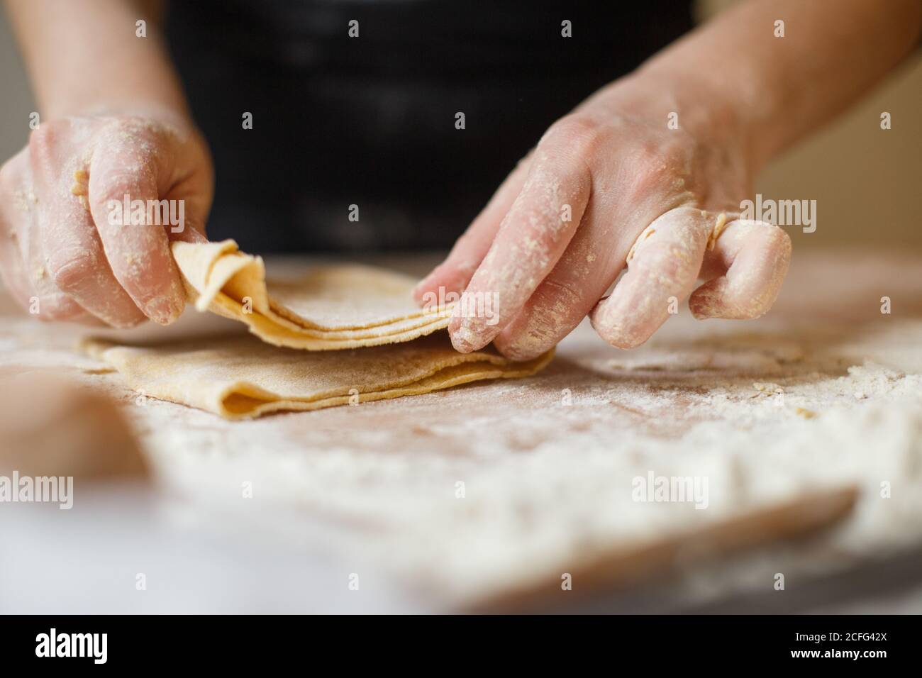 unrecognizable cook in black wear folding rolled thin pasta dough into ...