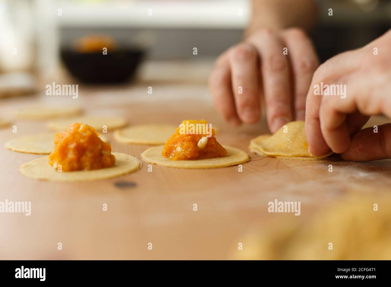 faceless cook pressing edges of pumpkin ravioli with fingers on table ...