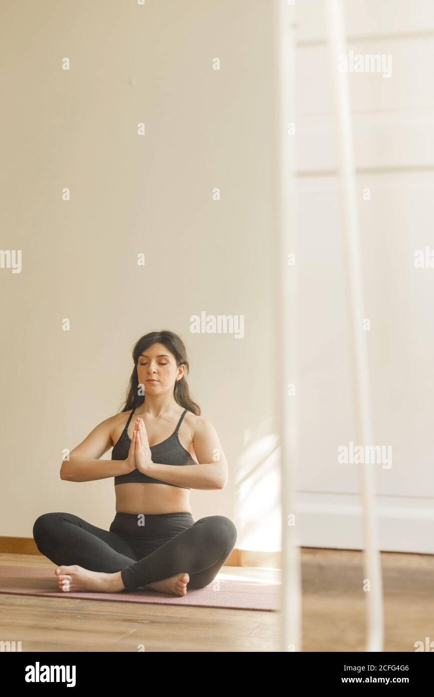 Focused female sitting on mat with closed eyes and Namaste gesture ...